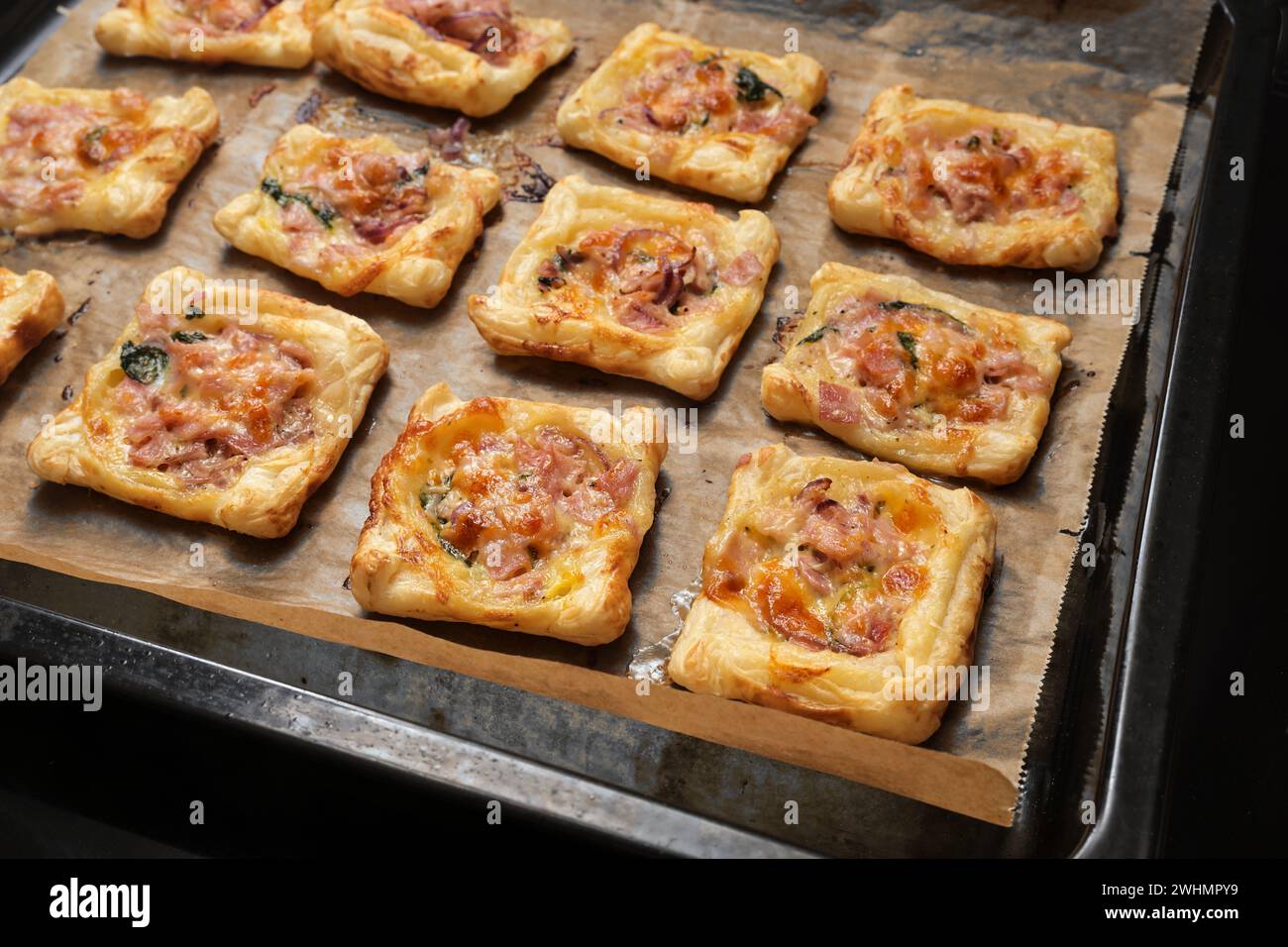 Baked puff pastry squares with ham, spinach and cheese on a tray with ...