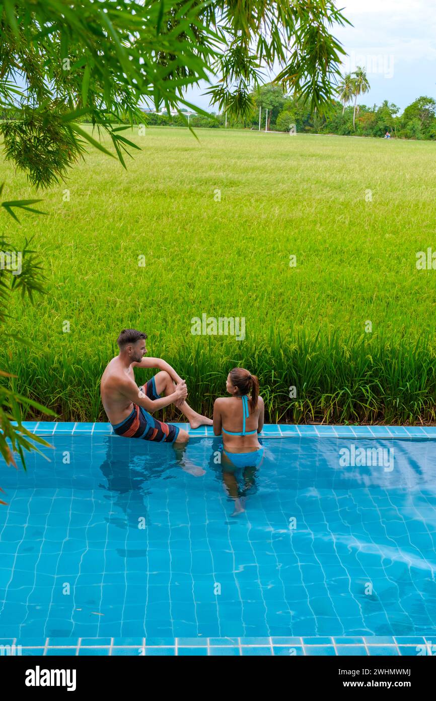 a couple of men and women in front of a Bamboo hut homestay farm, with Green rice paddy fields ...