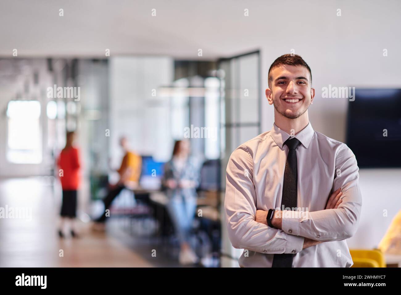A young business leader stands with crossed arms in a modern office ...