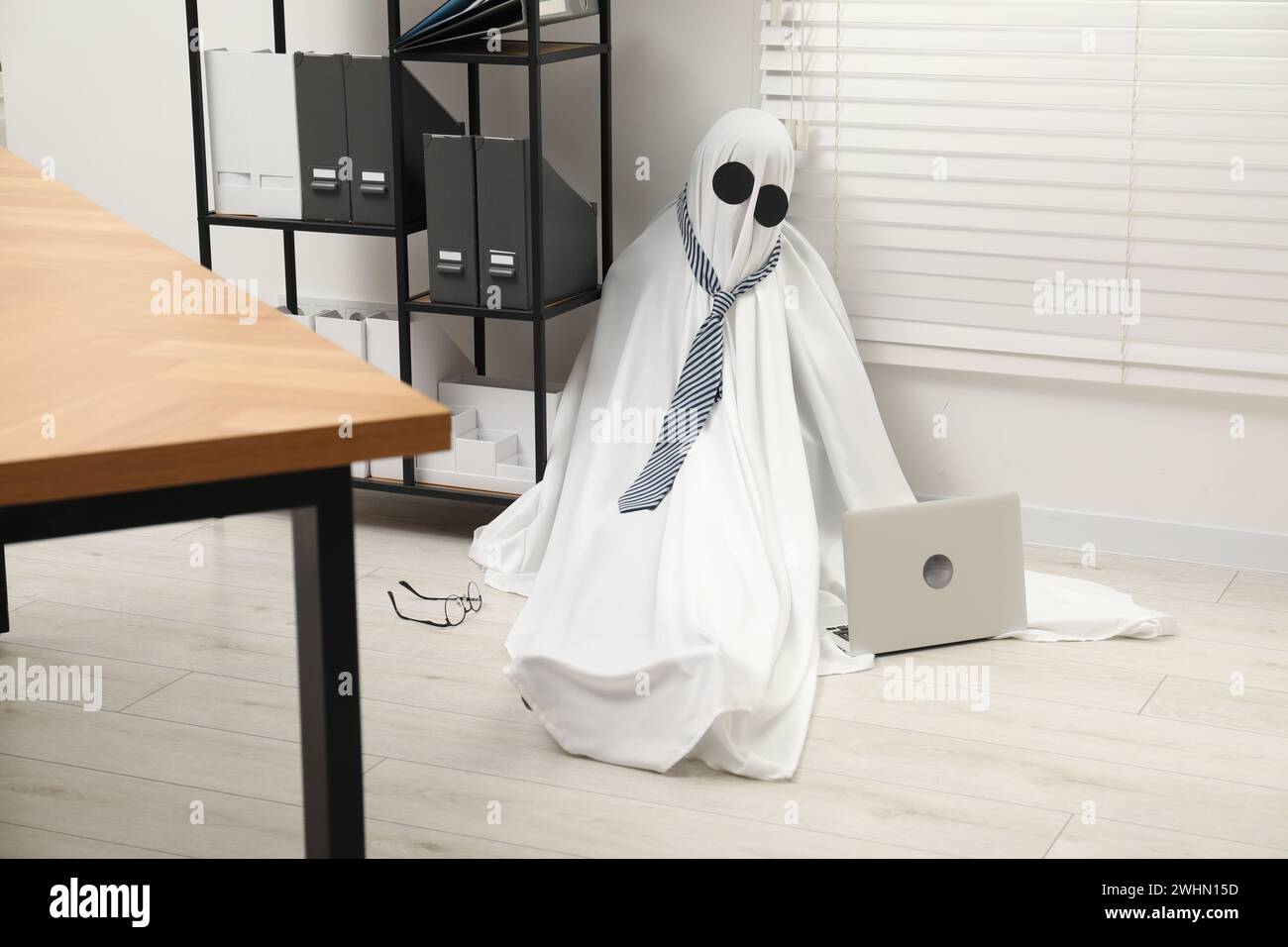 Overworked ghost. Man in white sheet with laptop on floor in office ...