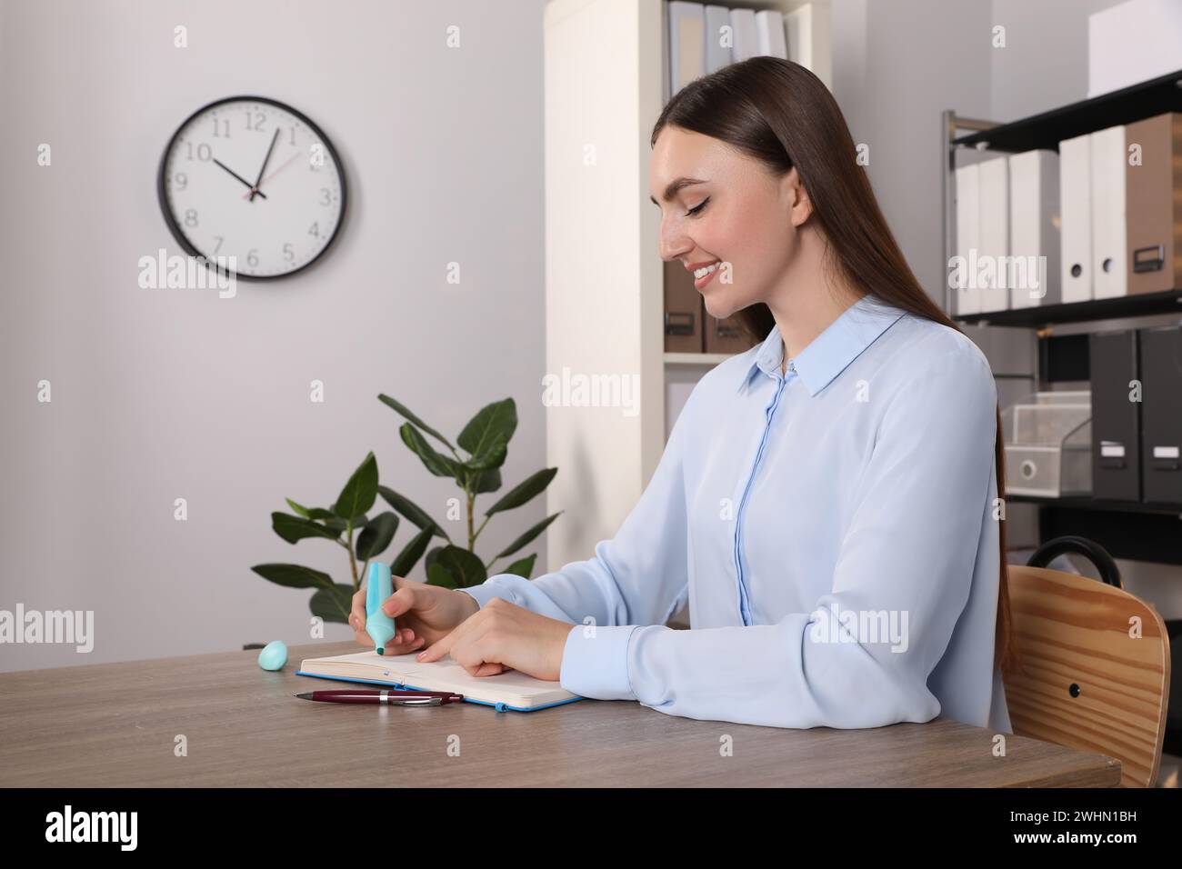 Happy woman taking notes at wooden table in office, space for text ...