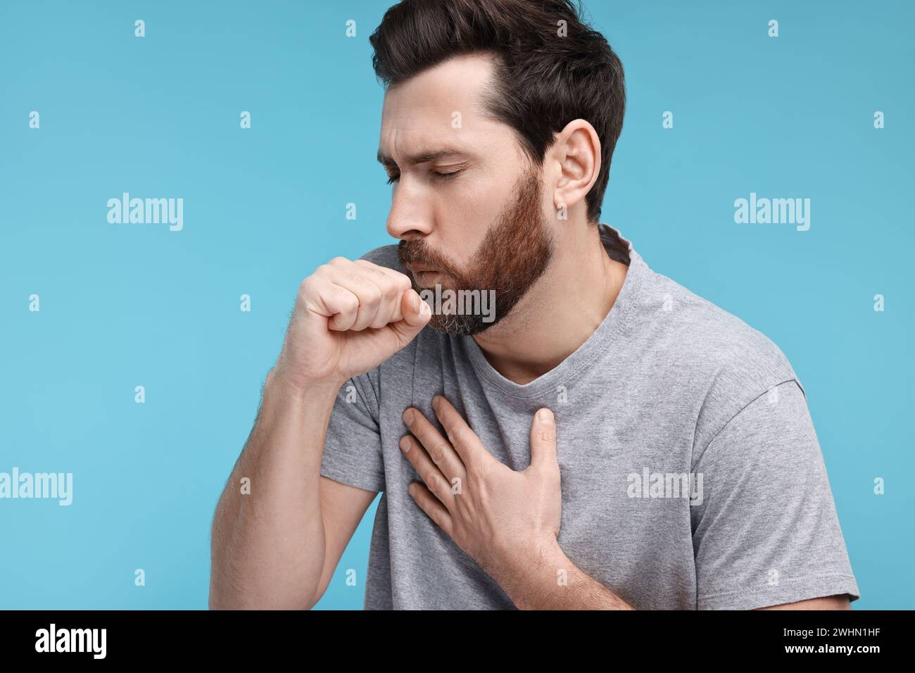 Sick man coughing on light blue background. Cold symptoms Stock Photo ...