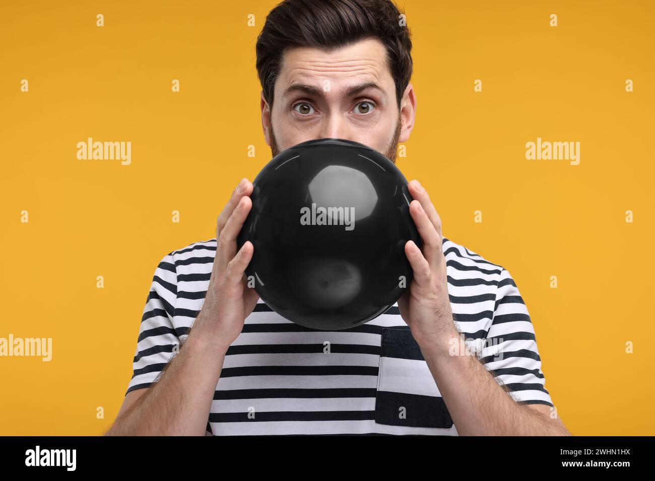 Man inflating black balloon on yellow background Stock Photo - Alamy