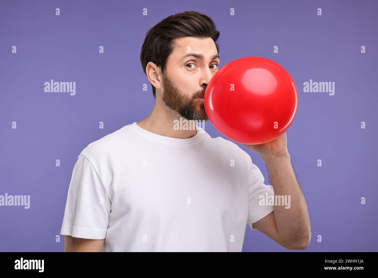 Man inflating red balloon on purple background Stock Photo - Alamy