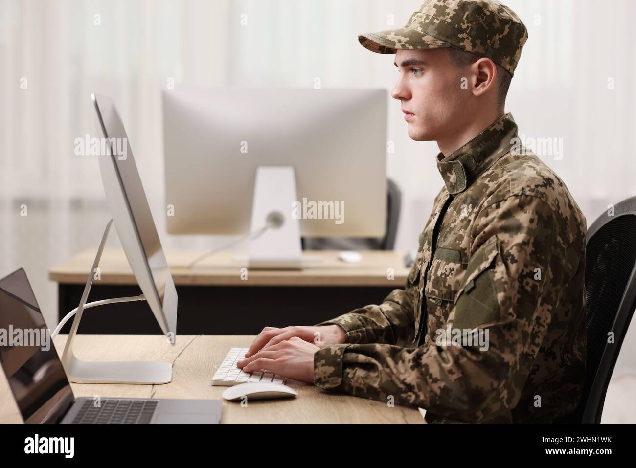 Military service. Young soldier working with computer at wooden table ...