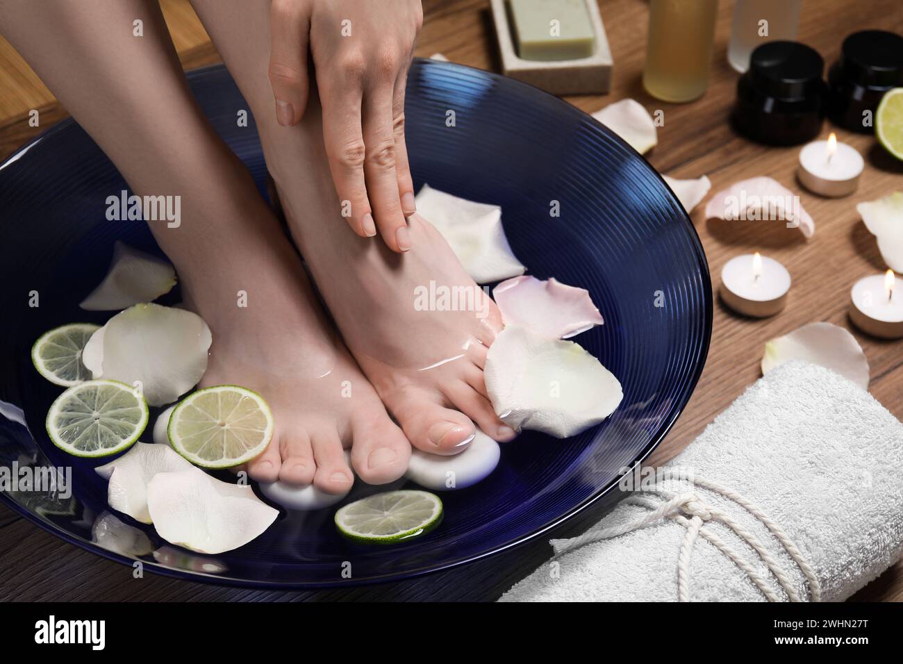Woman soaking her feet in bowl with water, petals and lime slices on ...