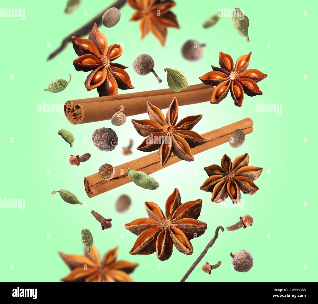 Different aromatic spices falling on green background Stock Photo - Alamy