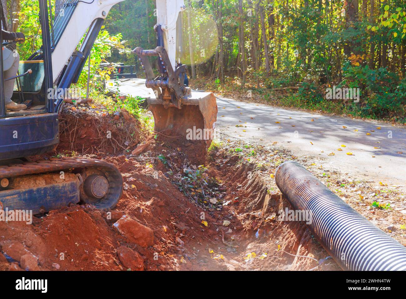 Trench is dug by an excavator for laying pipe through which rainwater ...
