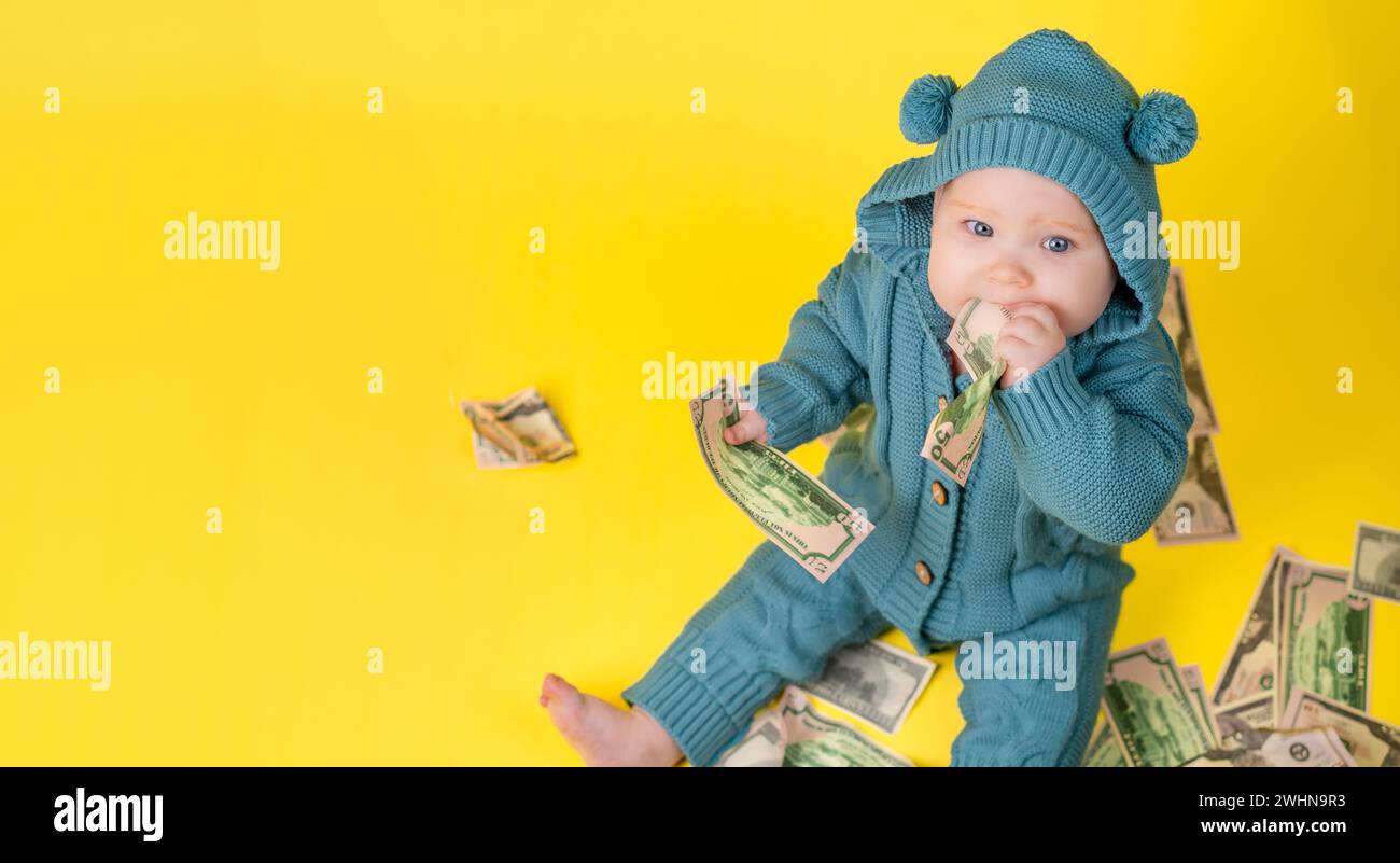 Baby in a blue knitted suit with money on a yellow background. Cute kid ...