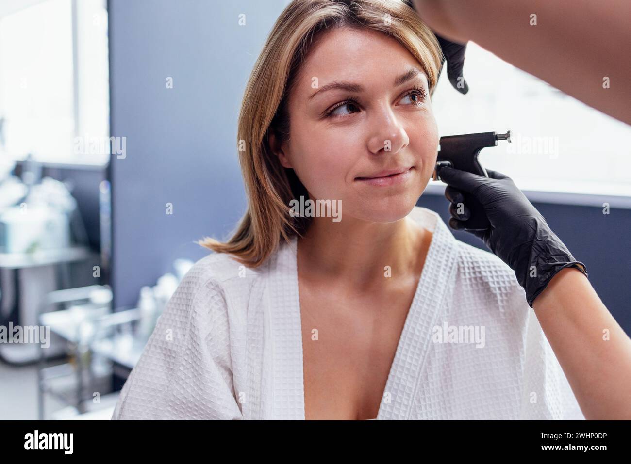Close up of face of young blonde woman doing ear piercing procedure ...