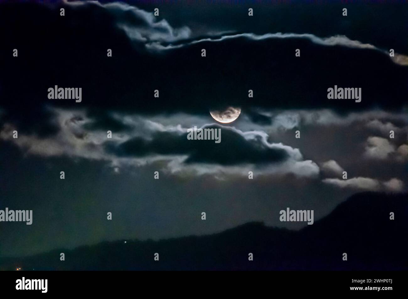 Full moon covered by clouds with profile of mountains Stock Photo - Alamy