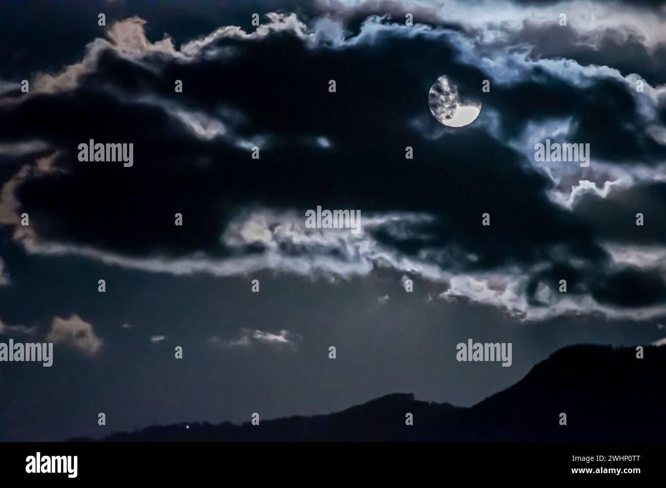 Full moon covered by clouds with profile of mountains Stock Photo - Alamy