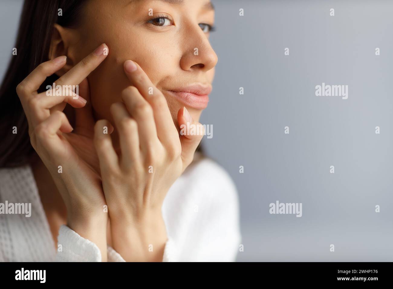 Attractive upset young woman in white bathrobe examines pimples on her ...