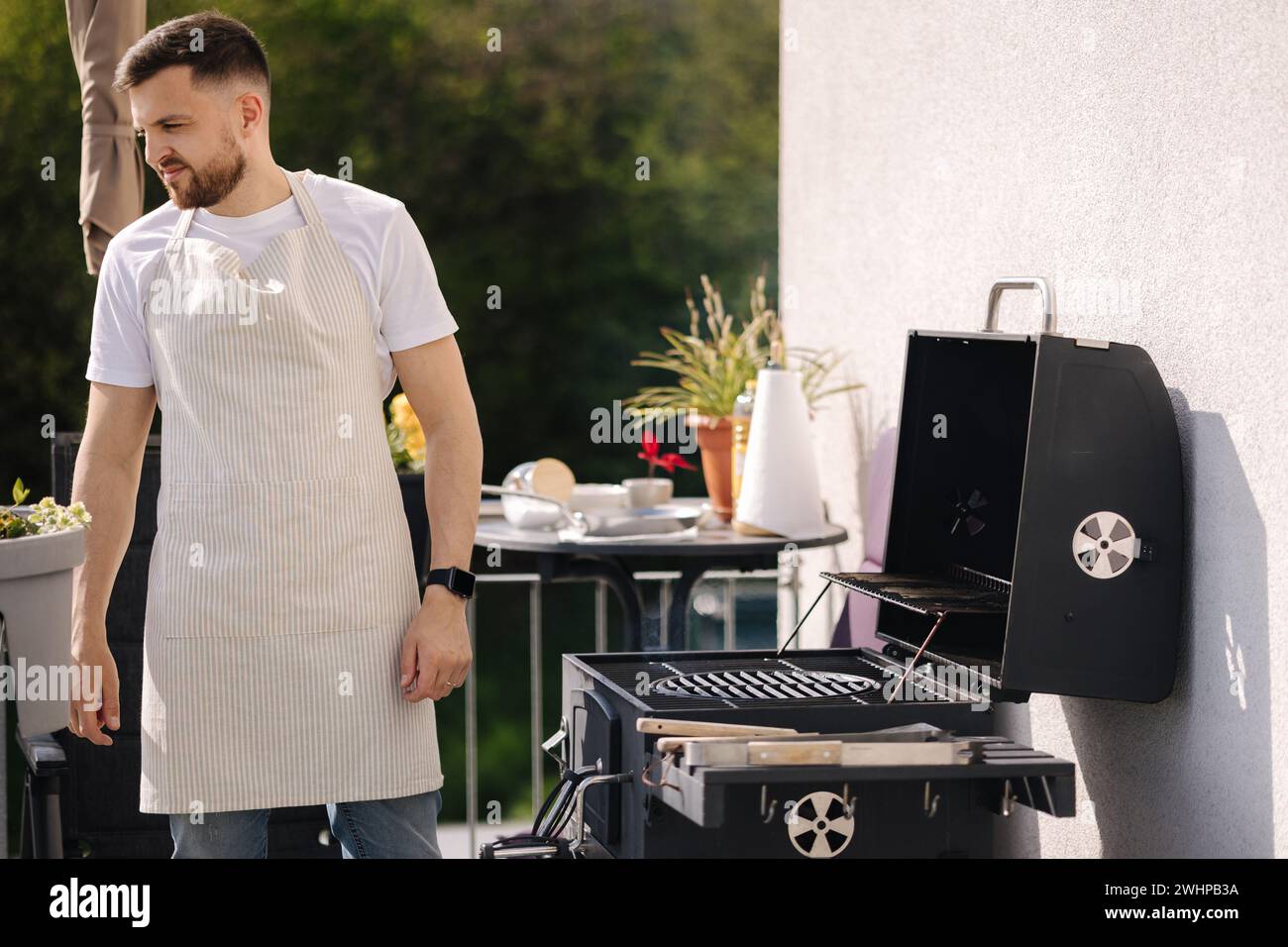 Side view of handsome man try how hot is BBQ grill. Man in apron make ...