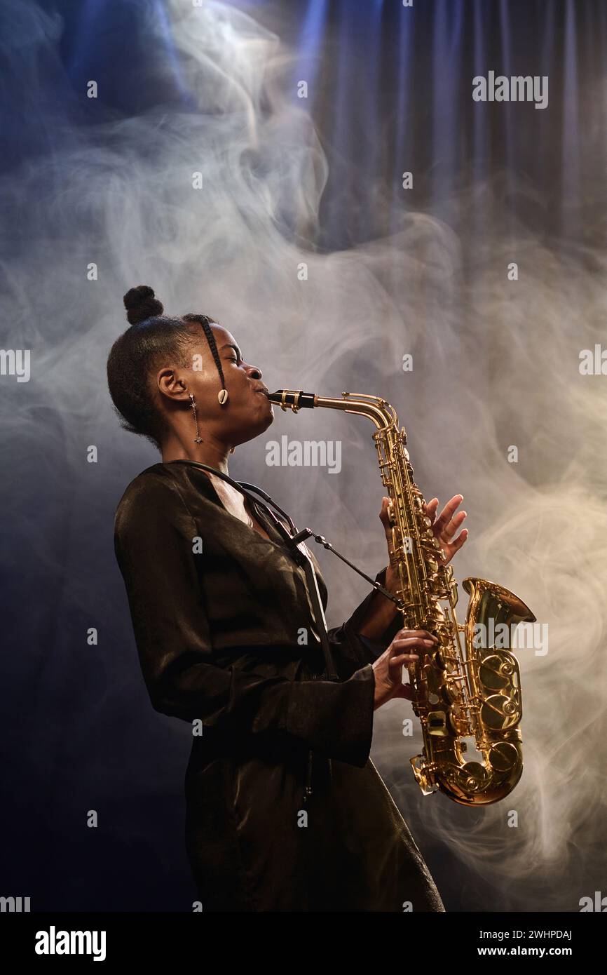 Vertical portrait of talented Black woman playing saxophone on stage during performance in jazz ...
