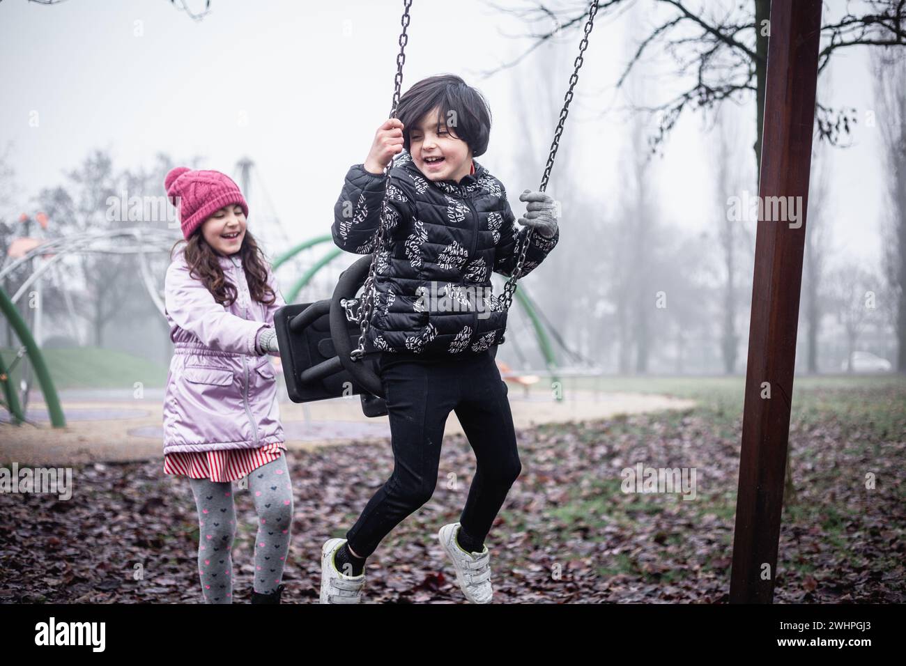 one happy girl pushing the one on the swing at children playground ...
