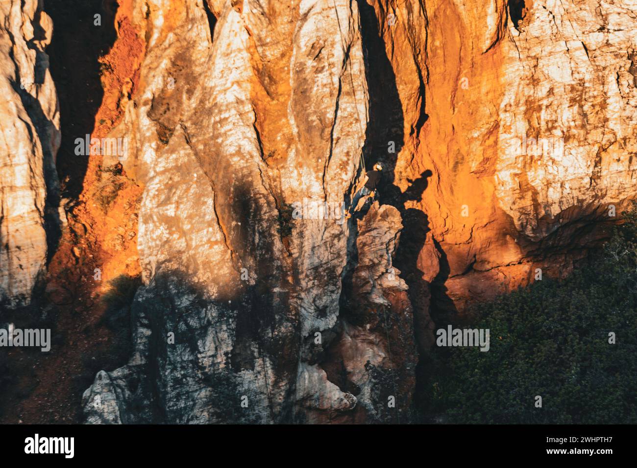 Man climber descends vertical rock face with lifeline and to rest mid ...