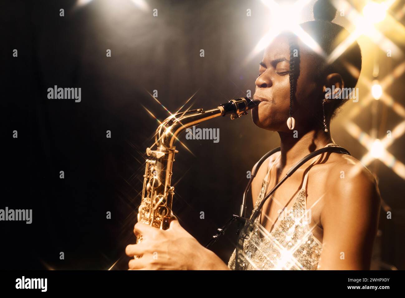 Side view portrait of young woman playing saxophone music on stage in ...