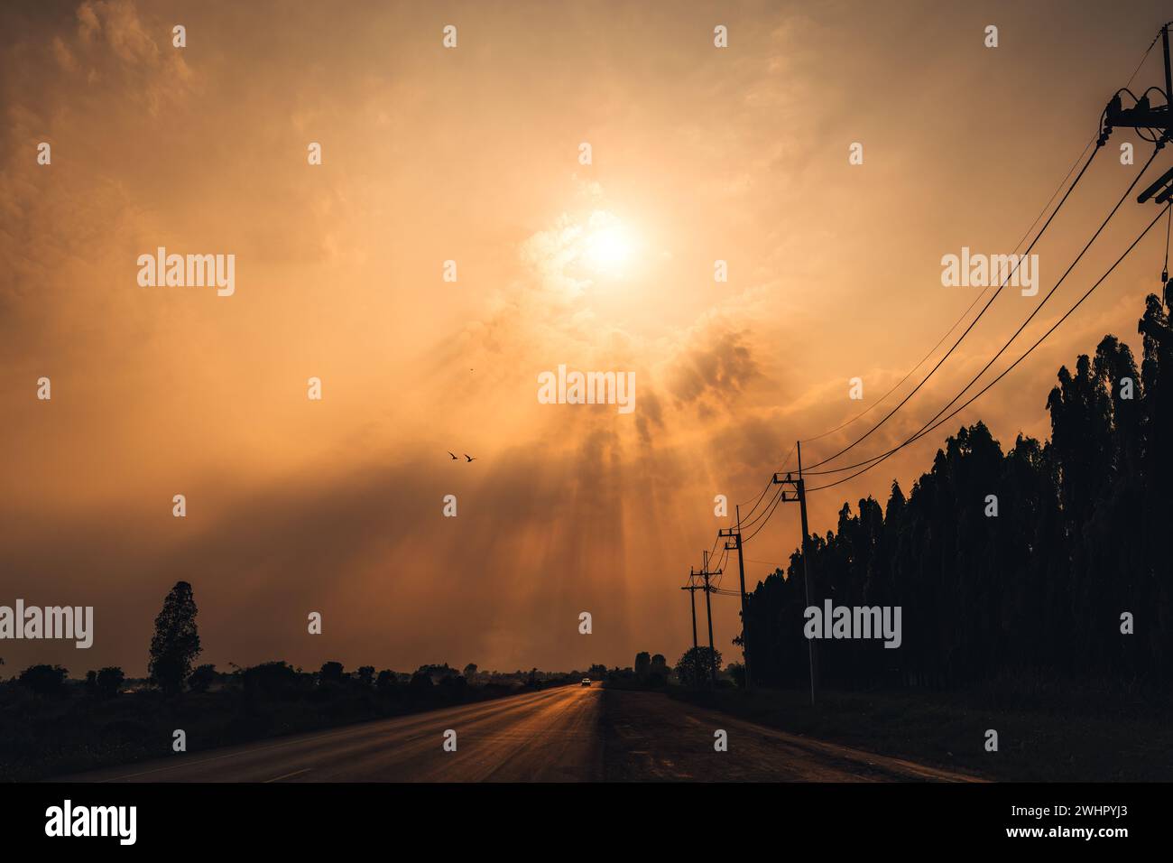 Dramatic golden sunset sky with sunbeam over rural road and eletricity ...