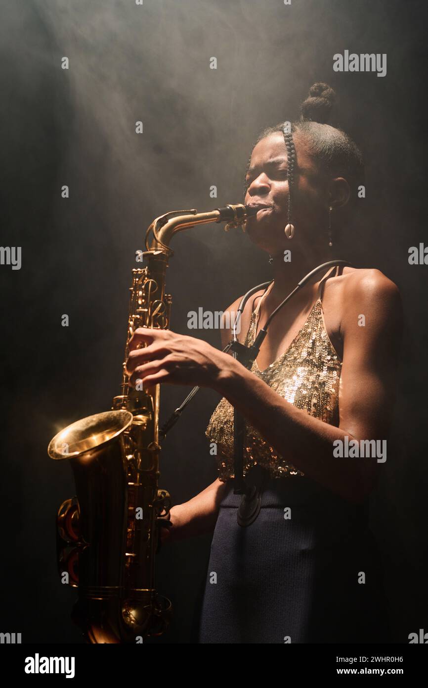 Side view portrait of young Black woman playing saxophone jazz music in ...