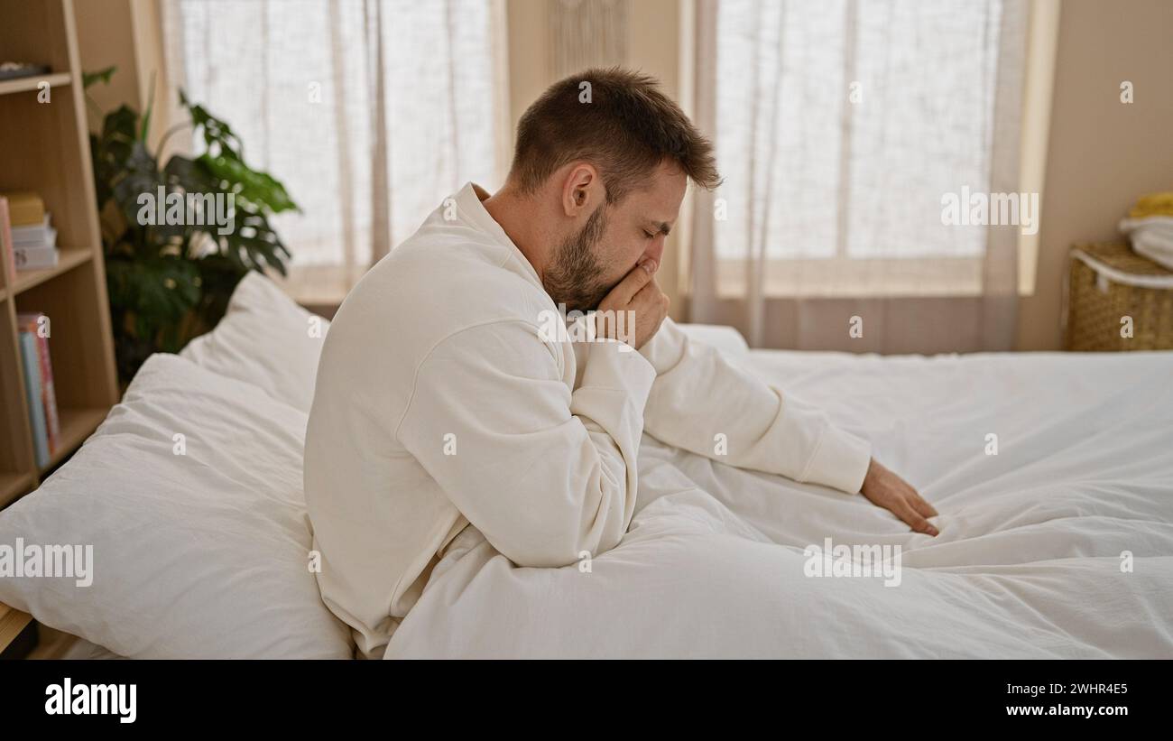 Exhausted young hispanic man, sitting restlessly on his bed, suffering ...