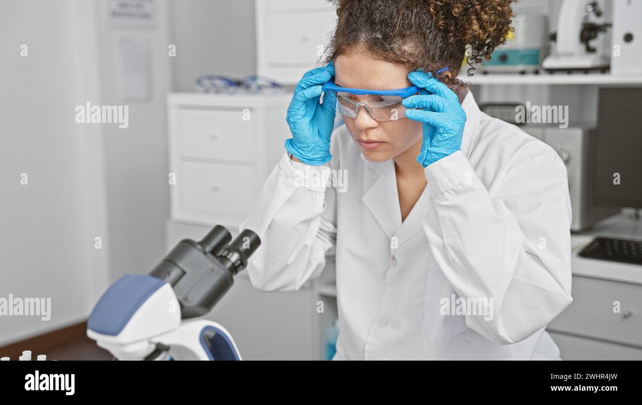 A Young Hispanic Woman Adjusting Goggles In A Laboratory Setting Embodying Professionalism And