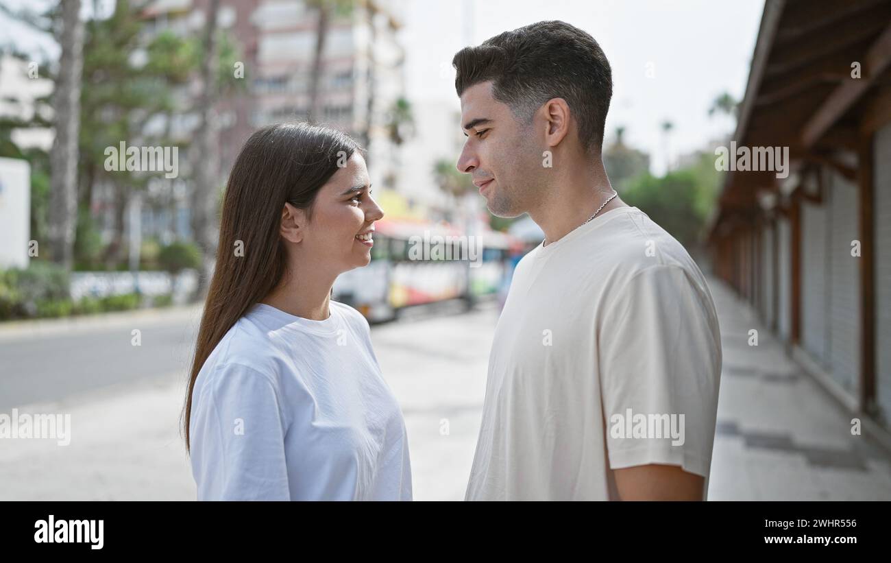 A smiling couple standing close together on a sunlit city street exudes ...