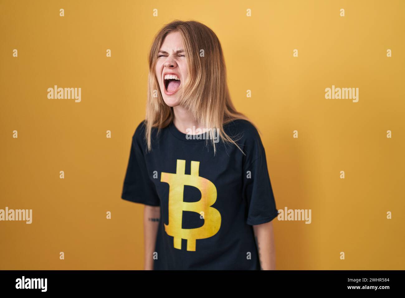 Blonde caucasian woman wearing bitcoin t shirt angry and mad screaming ...