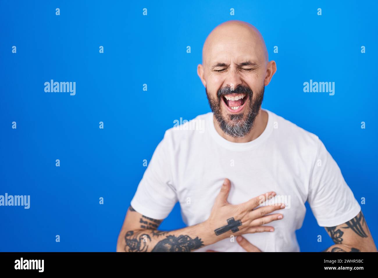 Hispanic man with tattoos standing over blue background smiling and ...
