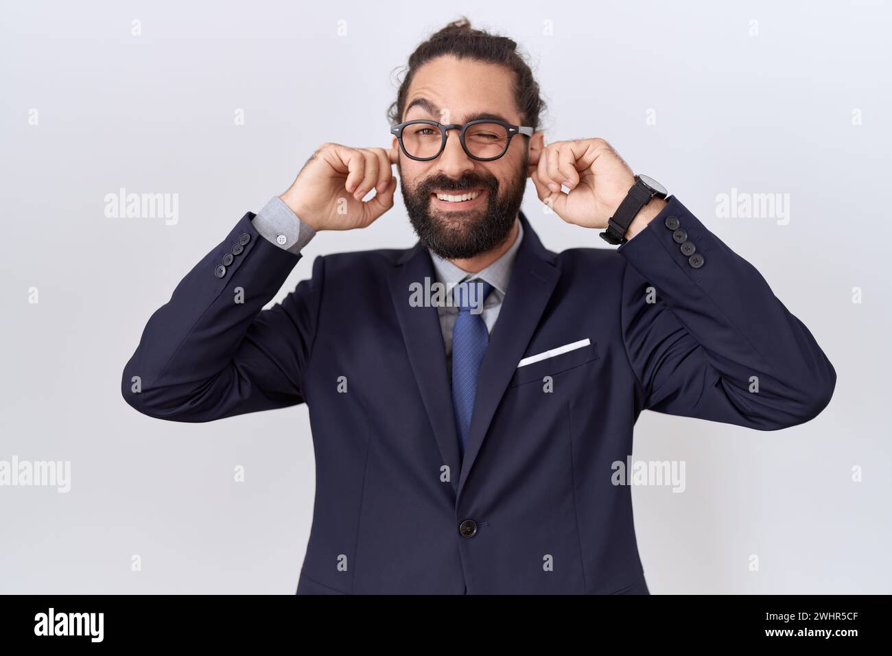 Hispanic man with beard wearing suit and tie covering ears with fingers ...
