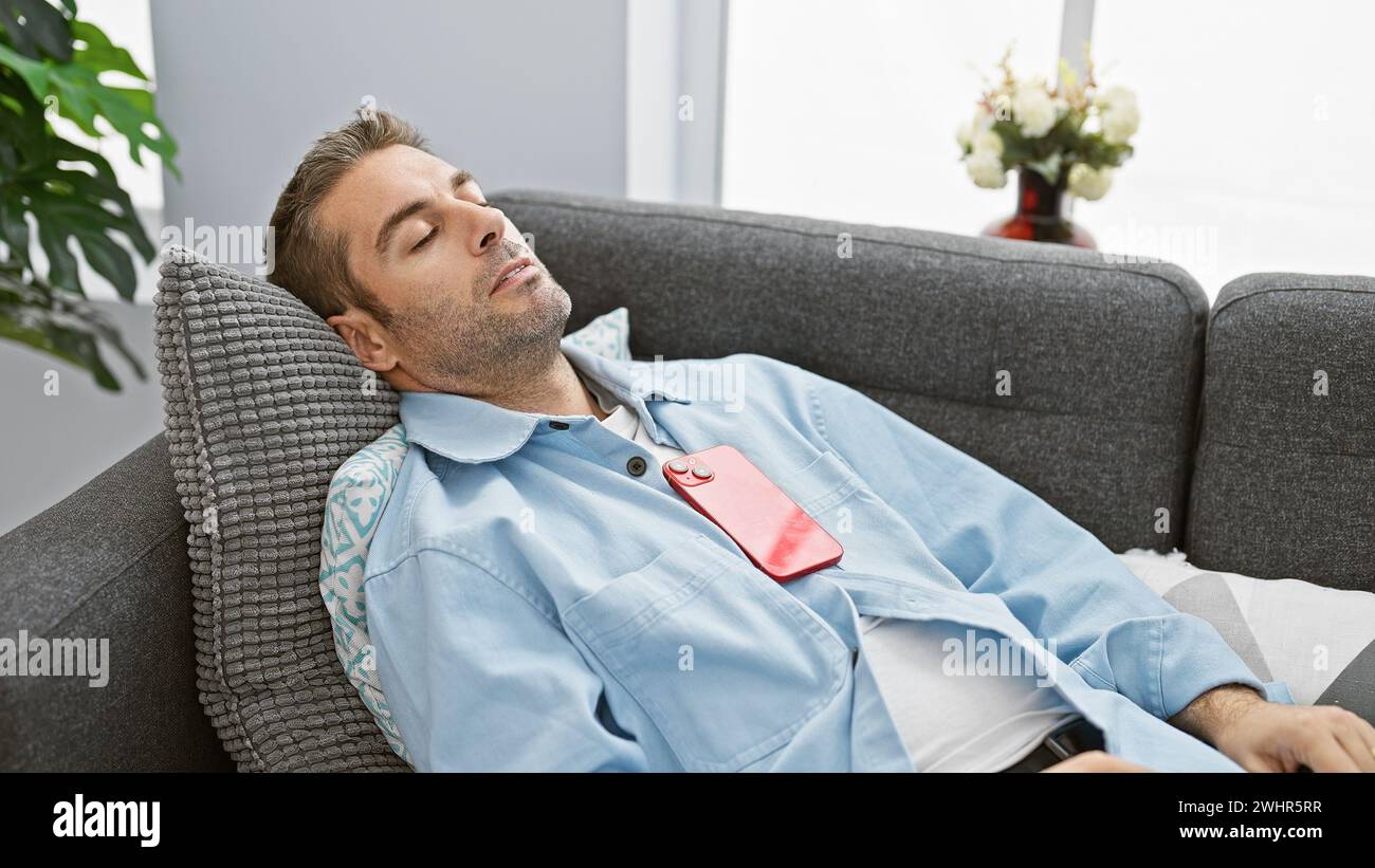 Handsome young man sleeping peacefully on a grey couch in a modern ...