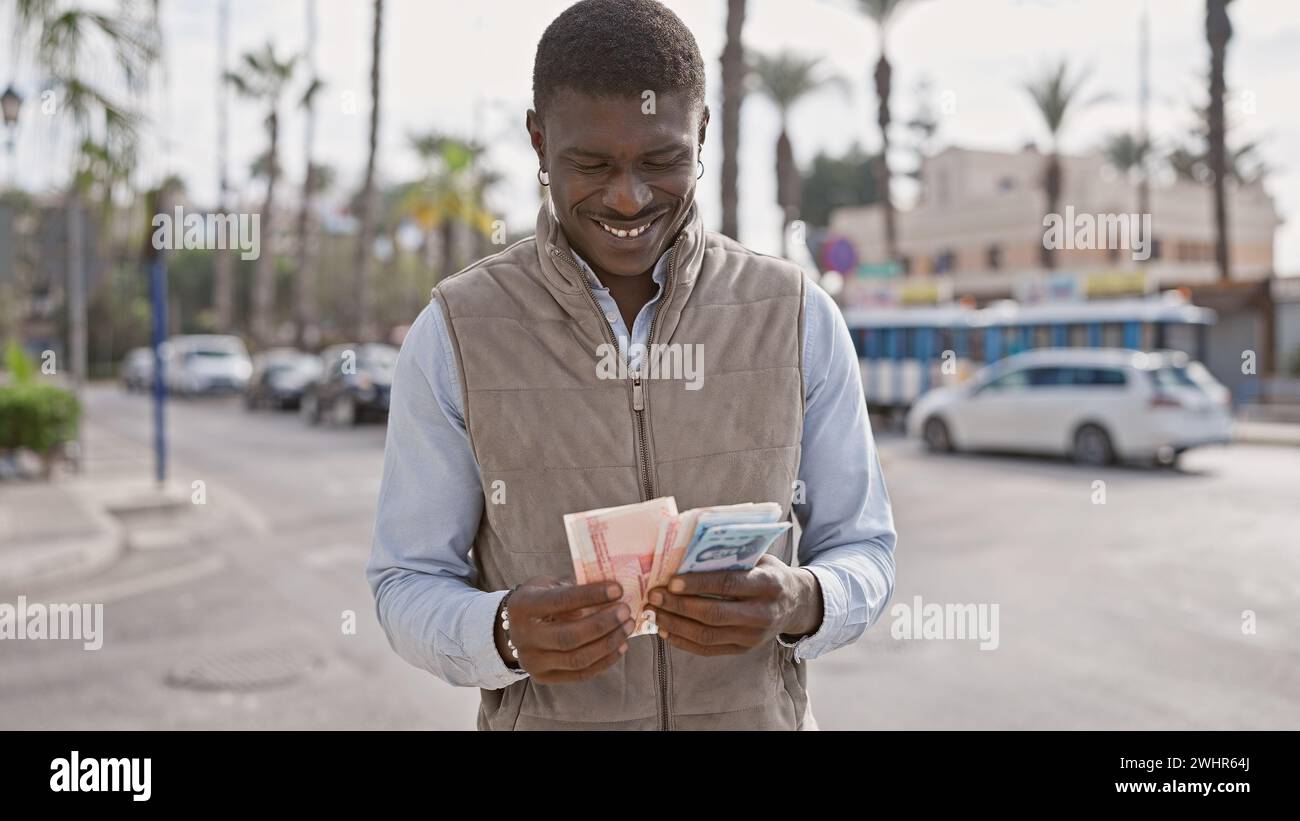 Smiling african man counting chinese yuan on a city street outdoors ...