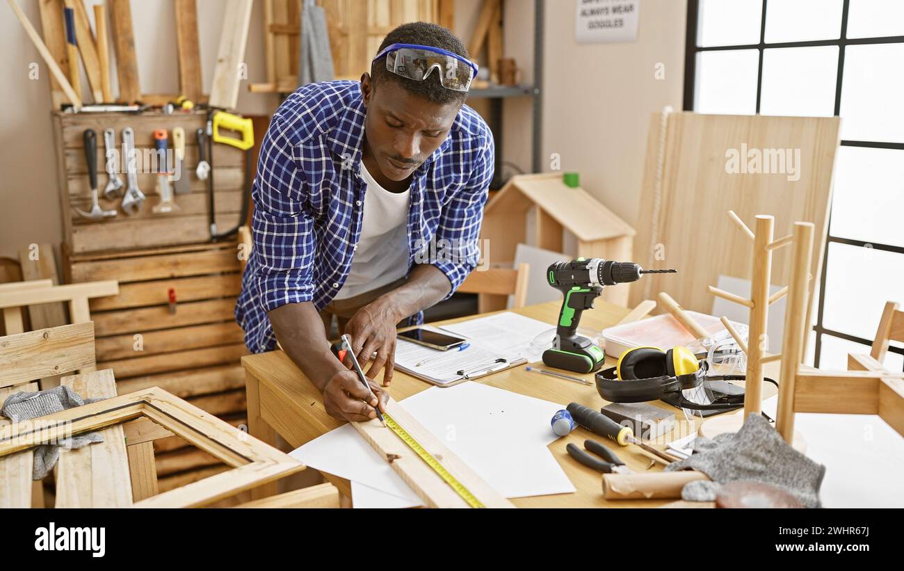 A skilled black man measures wood in an organized carpentry workshop ...