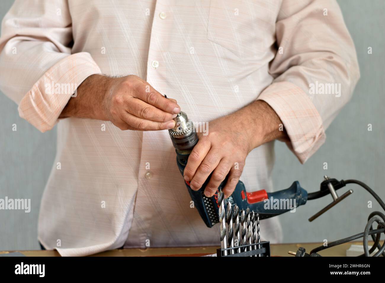 In the picture, a man who holds a drill with one hand, and clamps the ...