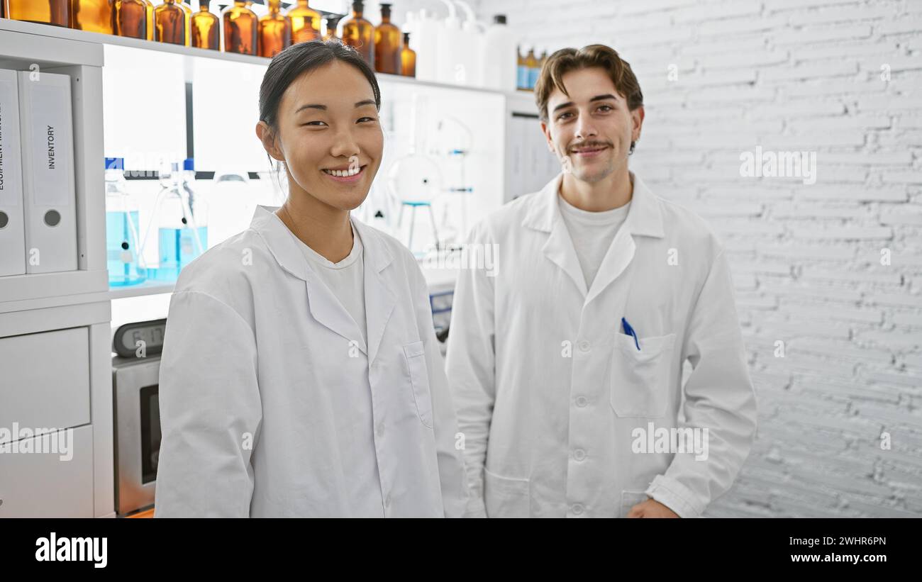 A man and woman in white lab coats stand smiling in a well-equipped ...