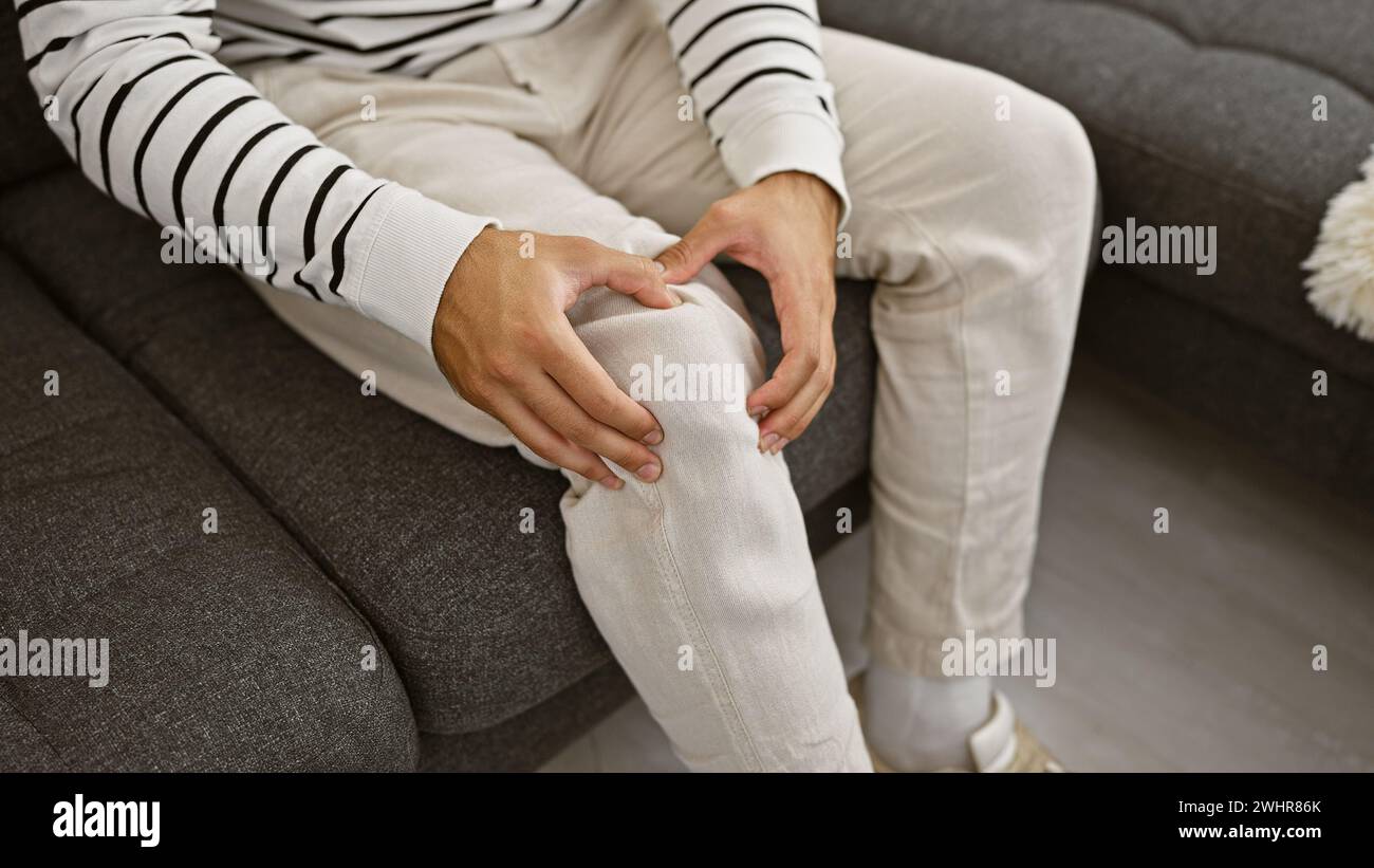 Hispanic man's hands gripping knee in pain, sitting on comfy living ...