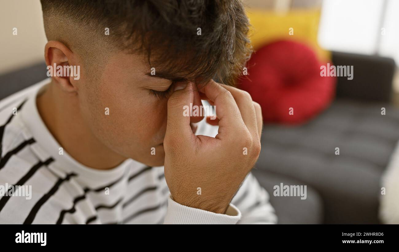 Stressed young hispanic man sitting alone on the sofa at home, feeling ...