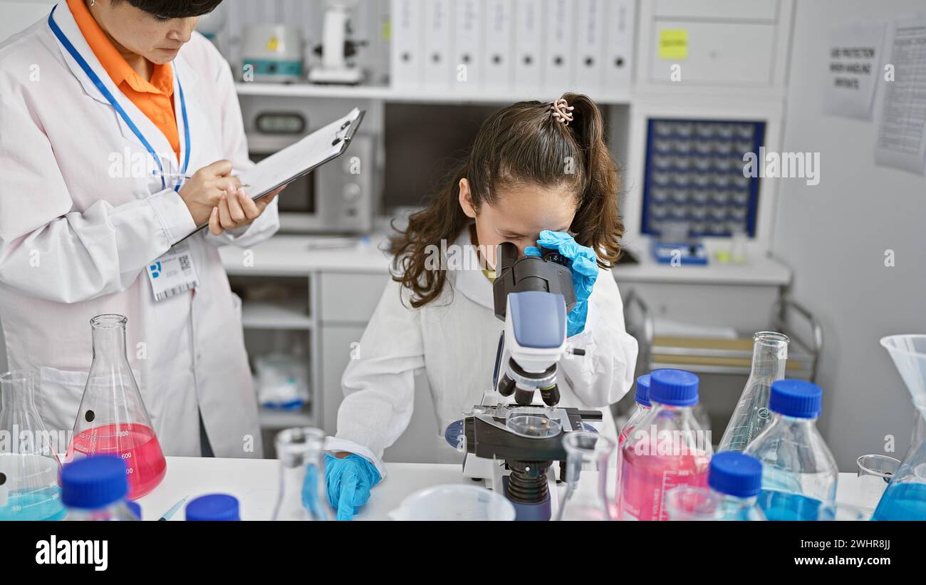 Two serious science girls, partners working together under microscope ...