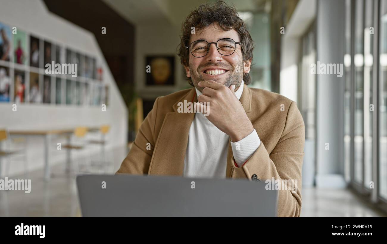 A cheerful young man with glasses and a beard working happily on a ...