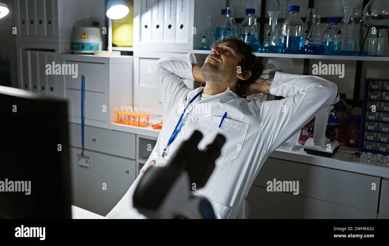 A tired young man in a white lab coat is taking a break in a chemistry ...
