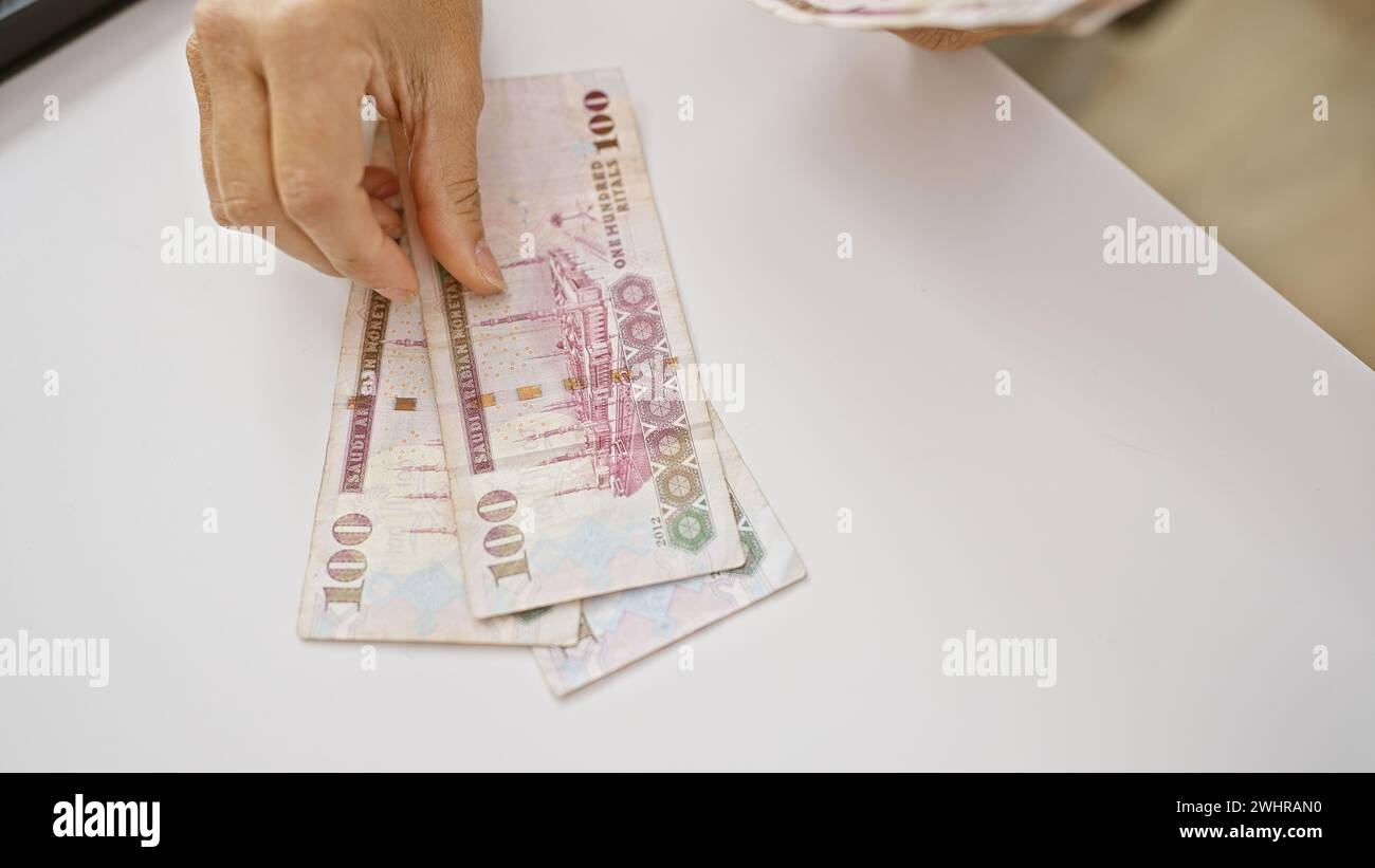 A woman's hands count saudi riyal banknotes at a white desk indoors ...