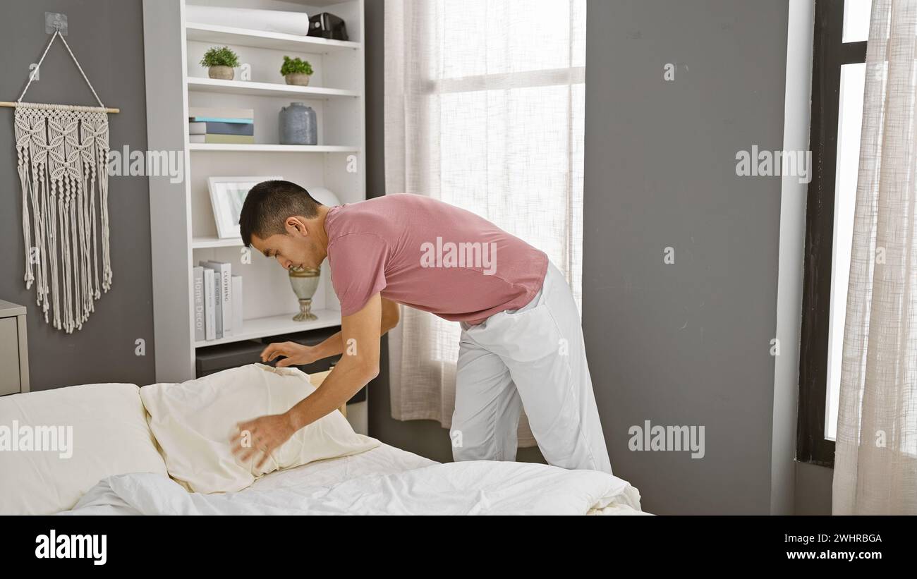 Young hispanic man making bed in a modern bedroom, showcasing daily ...