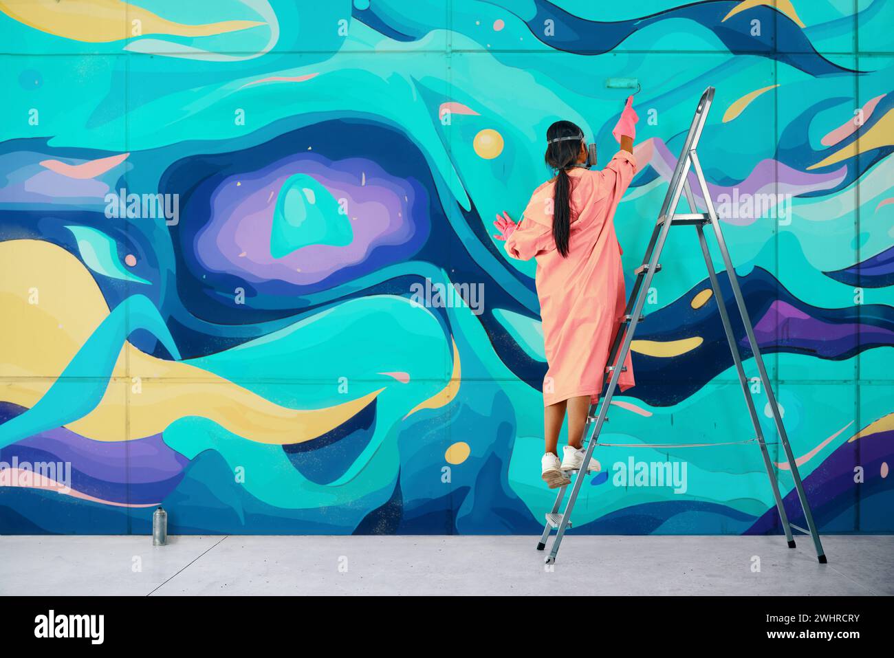 Female street artist painting colorful graffiti standing on a ladder ...