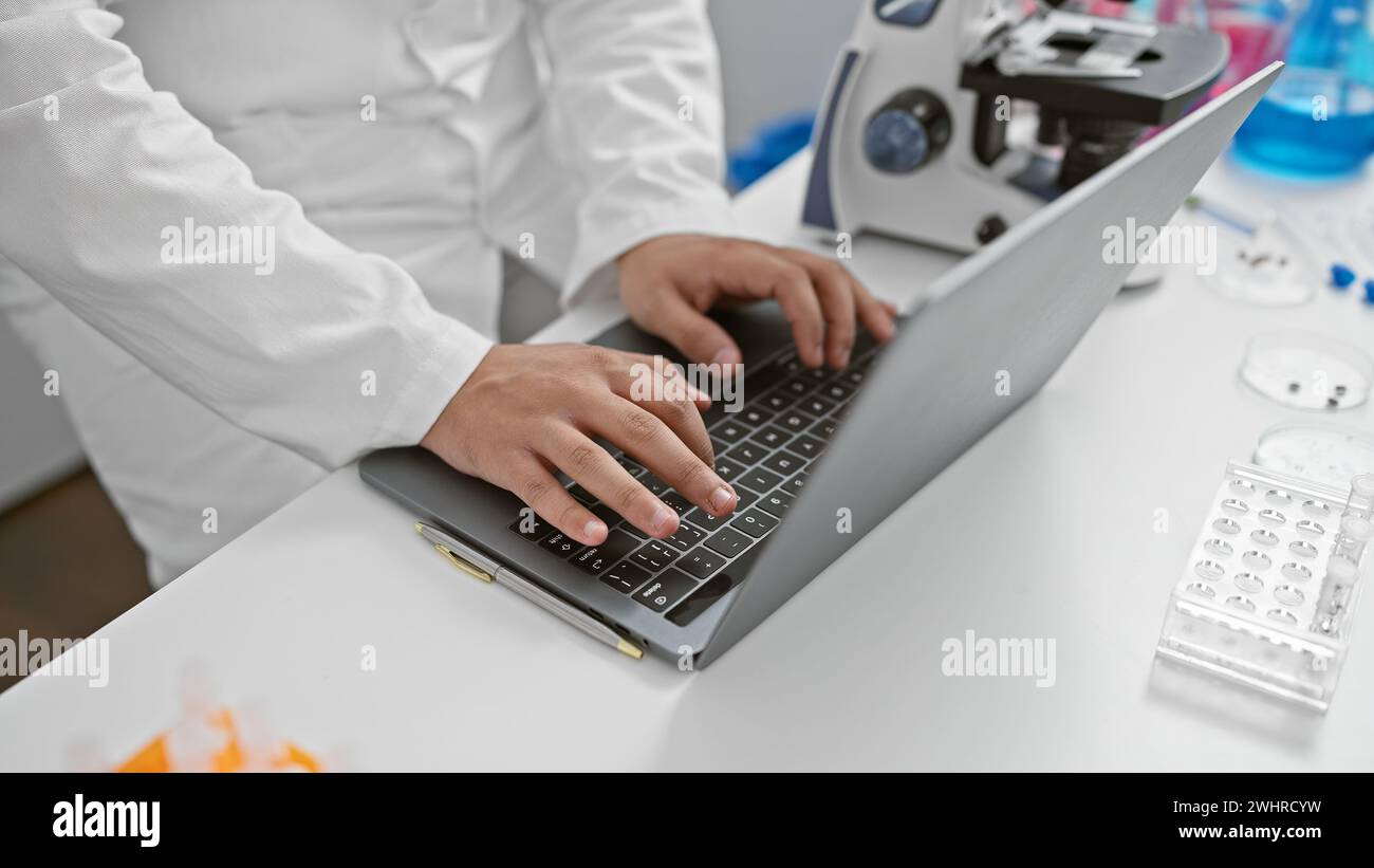 Scientist in lab coat using laptop in laboratory with microscope and ...