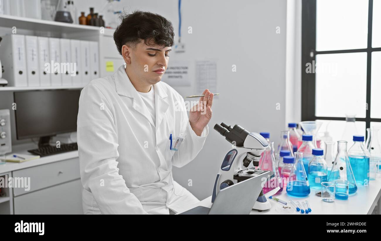 A young man in a white lab coat examines a pen while working with a ...