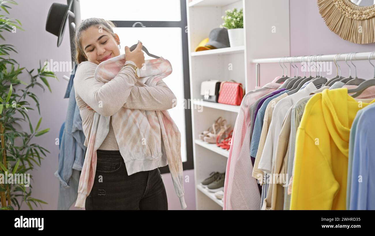 A happy hispanic woman hugging a jacket in a bright, modern dressing ...