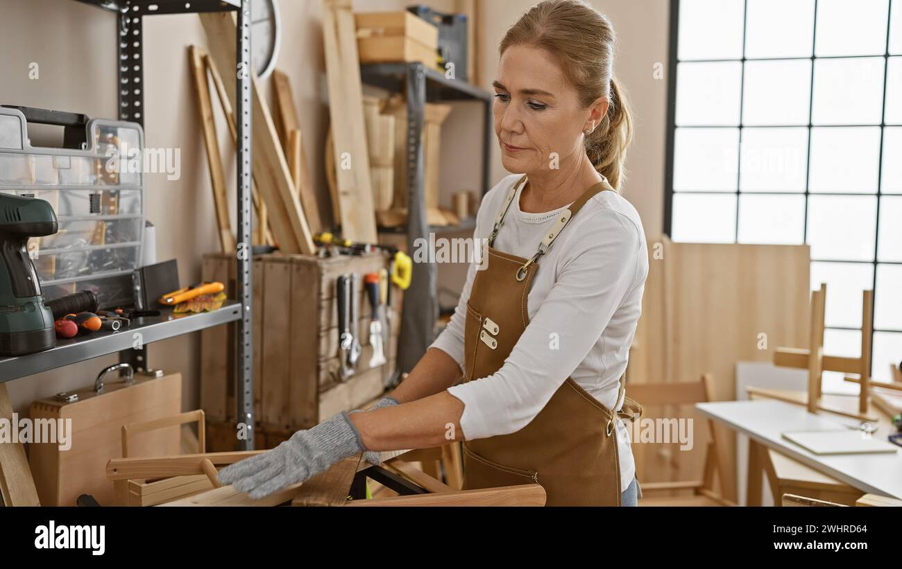 Mature blonde woman putting on gloves in a well-lit woodworking ...