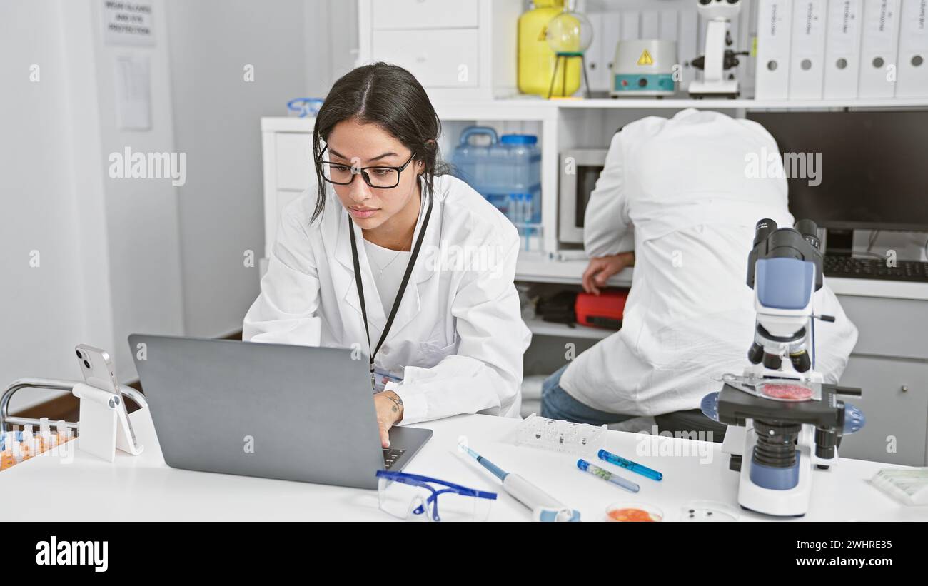 Woman and man scientists researching in laboratory with microscope, computer, and lab equipment ...