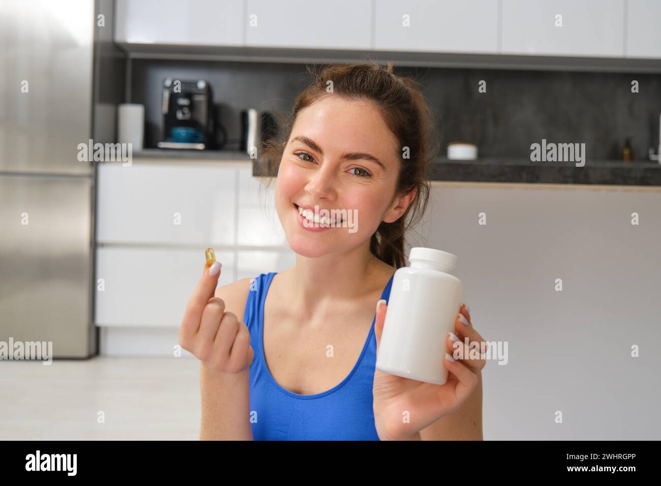Happy young fit girl, doing sports at home, shows dietary supplements ...