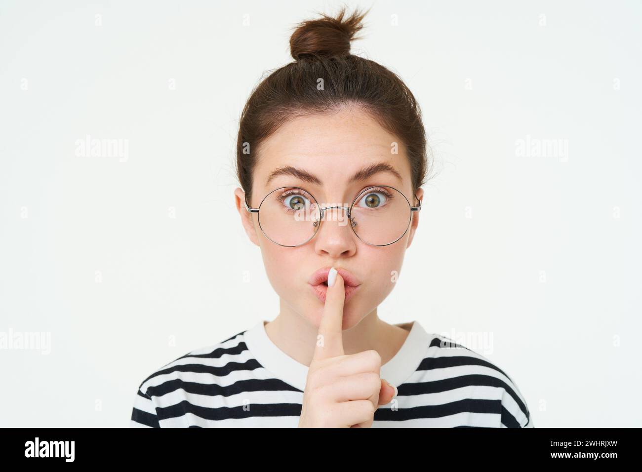Portrait of girl with glasses, looks surprised, hughing, press finger ...